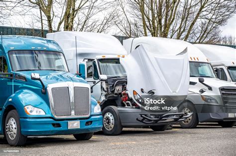 오픈 후드가 있는 흰색 대형 리그 세미 트럭은 주차된 다른 세미 트럭 옆 주차장에서 일상적인 검사 및 수리를 수행합니다 0명에
