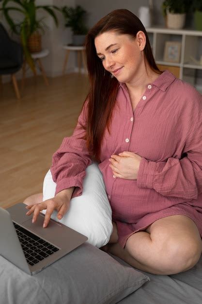 Mujer embarazada de tiro completo con computadora portátil en casa Foto Gratis