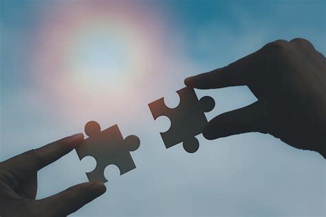 퍼즐 조각을 일출 배경과 연결하려고 하는 여자의 두 손 태양 광선과 하늘에 대한 퍼즐 나무 협회 팀워크 비즈니스 전략 및 연결의 상징 2명에 대한 스톡 사진 및 기타 이미지