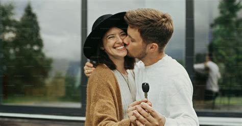 세련된 힙스터 커플이 테라스와 야외의 큰 창문을 배경으로 새 집의 열쇠를 들고 있습니다 행복한 젊은 가족이 키스를 하며 첫 번째 부동산 구입을 축하합니다 사진