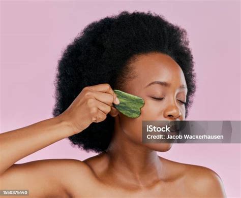 Gua Sha 마사지 및 자연의 아름다움 얼굴 관리 및 피부가 분홍색 배경에 빛나는 흑인 여성 여성 모델 옥 화장품 도구 및 스튜디오에서 아프로 헤어와 얼굴 스킨케어가 있는