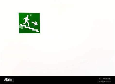 A Green Sign Down The Stairs On An Empty Bright Wall DIRECTION TO THE EMERGENCY EXIT ON THE