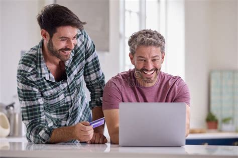 Same Sex Male Couple With Credit Card Using Laptop At Home To Book Holiday Or Shop Stock Image