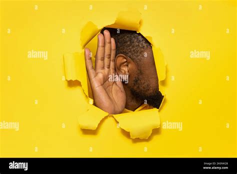 Black Mans Ear And Hand Through A Torn Hole In Yellow Paper Background Free Copy Space