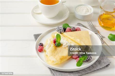 전통적인 얇은 팬케이크 또는 크레페와 코티지 치즈 건포도 열매 꿀 사워 크림이 흰색 나무 배경에 있습니다 마레그나에 대한 음식