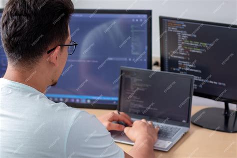 Premium Photo A Young Programmer Wearing Glasses Working With Three Monitors Writing
