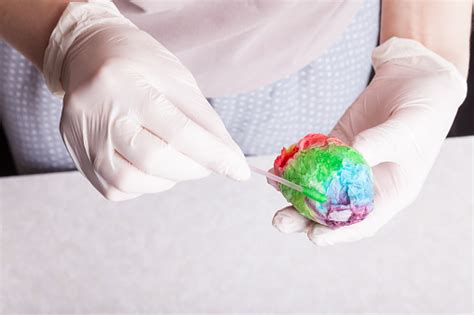 라텍스 장갑에 가까운 여성의 손을 클로즈업 흰색 테이블의 배경에 냅킨에 싸여 면 봉면을 사용하여 다른 색상의 염료를 적용 부활절 달걀을 색칠하는 새로운 디자인 건조한에 대한