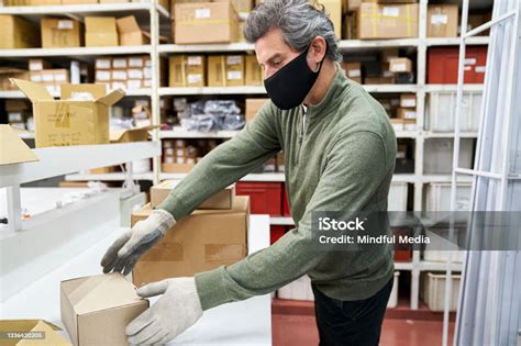 실내 포장 테이블 옆에 서있는 동안 골판지 상자를 들고 남성 저장 실 운영자의 측면 보기 40 44세에 대한 스톡 사진 및 기타