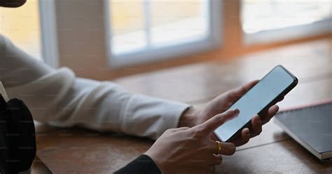 흰색 빈 화면 스마트폰을 들고 있는 세련된 여성의 손이 편안한 거실 창문 위에 있는 나무 작업 책상에 앉아 휴식을 취하는 동안 자른 이미지 사진 Unsplash의