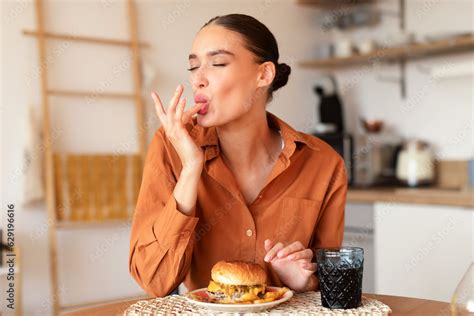 Contented Caucasian Lady Licking Her Fingers While Eating Delicious French Fries And Hamburger
