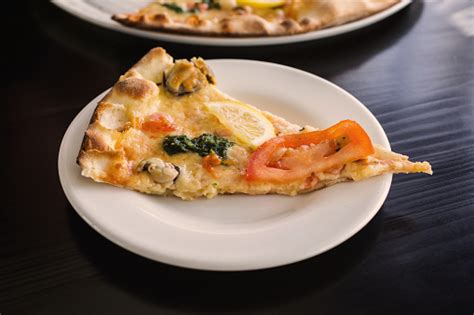 흰색 도자기 접시에 해산물 허브 치즈 토마토 레몬 조각과 황금 향기로운 피자의 조각 블랙 테이블에 이탈리아 국가 접시 재료의 많은 작품의 케이크 높은 칼로리 식품 자연