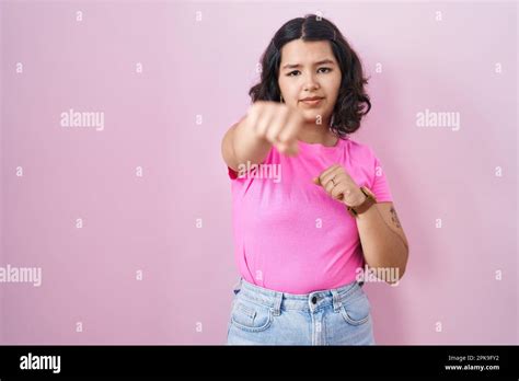 Young Hispanic Woman Standing Over Pink Background Punching Fist To