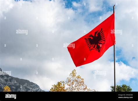 Red Albanian Flag With Double Headed Black Eagle Flutters In The Wind On Blue Sky Background