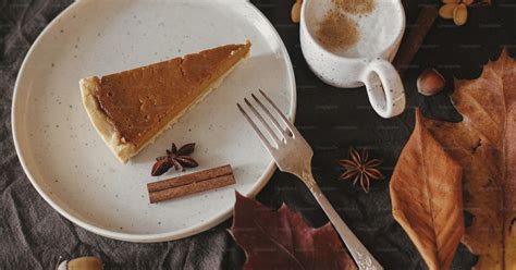 현대적인 접시에 호박 파이 슬라이스와 린넨 냅킨 가을 꽃과 잎 아니스와 계피가 있는 소박한 테이블에 뜨거운 커피 수제 호박 타르트 레시피 평면도 행복한 추수 감사절