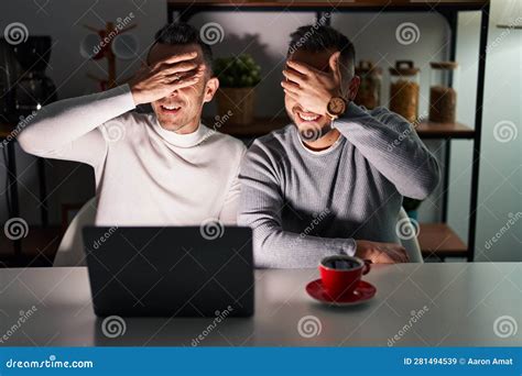 Homosexual Couple Using Computer Laptop Smiling And Laughing With Hand On Face Covering Eyes For