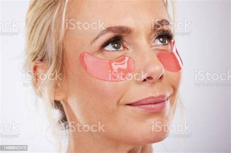 스킨케어 콜라겐 아이 마스크 노화 방지 치료를 받은 성숙한 여성이 스튜디오의 회색 배경에 고립되어 있다 건강 피부 미용 미소를 짓고 얼굴에 패치를 붙이고 고급 스파 페이셜을