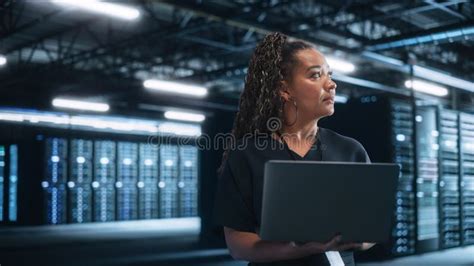 Mixed Racefemale It Specialist Uses Laptop Computer In Data Center Server Farm Cloud Computing
