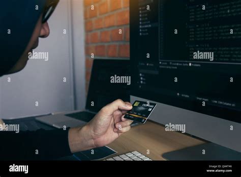 Hacker In The Hood Working With Computer And Holding Credit Card With