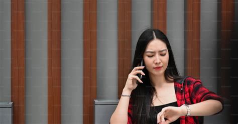 젊은 여자는 도시에서 야외에 서 있는 동안 휴대전화로 이야기하고 손목 시계로 시간을 확인합니다 사진 Unsplash의 태국 이미지