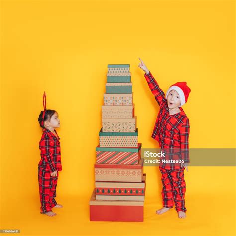 노란 배경에 맞서 크리스마스 선물 옆에 서 있는 빨간 잠옷을 입은 아이들 12월에 대한 스톡 사진 및 기타 이미지 12월 2 3 살 2명 Istock