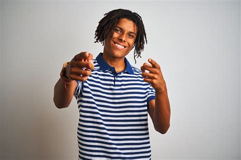 행복하고 재미있는 얼굴로 카메라에 손가락을 가리키는 고립 된 흰색 배경 위에 서있는 줄무늬 파란색 폴로를 입은 공포를 가진 아프로 남자 좋은 에너지와 분위기 가리키기에 대한