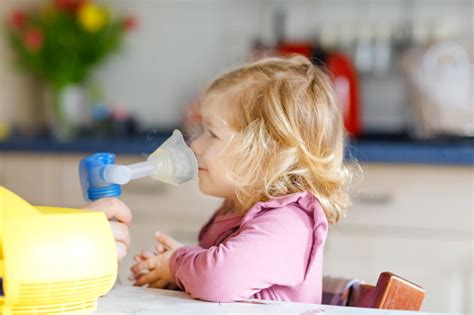 집에서 분무기로 흡입을 만드는 작은 유아 소녀 아버지 또는 어머니는 장치를 돕고 들고 독감 기침 및 기관지염을 가진 아이 천식 흡입기 흡입 증기 아픈 개념 건강관리와 의술에