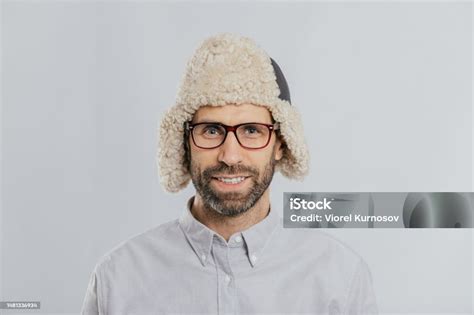 쾌활 한 잘생긴 백인 남자의 얼굴만 Earflaps 안경 및 흰 셔츠와 함께 따뜻한 겨울 모자를 착용 카메라 야외 산책 흰색 배경 위에 절연에 대 한 준비에 직접 안경류에