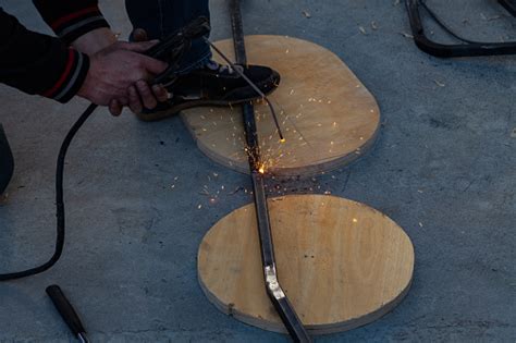 클로즈업 보기 강한 남자는 팔에 장갑 없이 파란색 작업 바지에 용접기 금속 제품은 차고 워크샵에서 용접 기계로 용접 블루 연기와