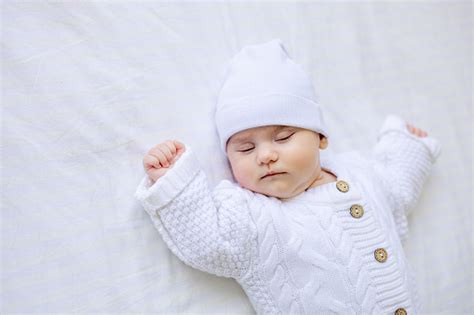 신생아는 흰색 따뜻한 점프수트를 입고 유아용 침대에서 자고 흰색 단열 면 침대에 모자를 쓰고 건강한 아기 수면 클로즈업 2 5