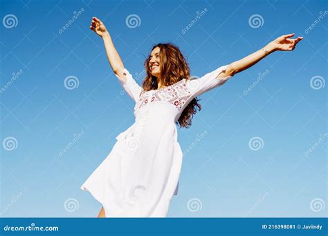 νεαρή γυναίκα σηκώνει τα χέρια της με ένα όμορφο λευκό φόρεμα ενάντια στον γαλάζιο ουρανό Στοκ