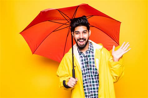 오렌지 배경 에 비에서 빨간 우산 커버와 노란색 비옷에 젊은 잘 생긴 수염 인도 남자 가을에 대한 스톡 사진 및 기타 이미지 가을 귀여운 날씨 Istock