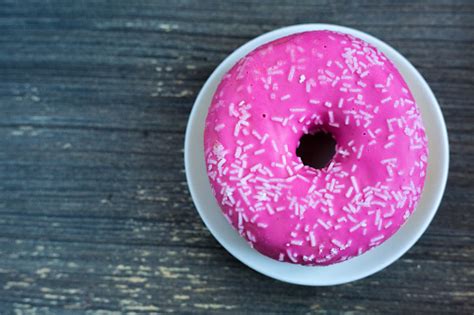 하얀 둥근 접시와 오래된 나무 회색 배경에 밝은 분홍색 도넛을 올려 놓으십시오 격리된 개체가 닫힙니다 아침 식사로 전통적인 미국