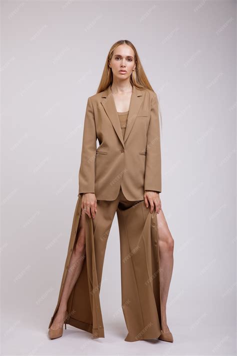 베이지색 갈색 정장 바지를 입은 여성이 솔기 재킷에서 단추를 풀고 흰색 배경 스튜디오 샷 프리미엄 사진