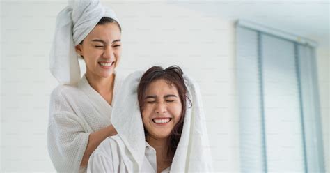 아시아의 아름다운 레즈비언 커플이 함께 아침 여가 시간을 보내고 있다 잠옷을 입은 매력적인 낭만적인 소녀가 집 침실의 침대에서 샤워를 한 후 여자 친구의 머리카락을 말리고