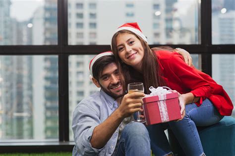 재미와 크리스마스 파티와 사랑에 젊은 부부 샴페인 유리 Ang 포옹 예쁜 여자를 들고 백인 잘 생긴 남자 산타 모자를 입고 선물 상자를 들고 새해 12월에 대한 스톡 사진