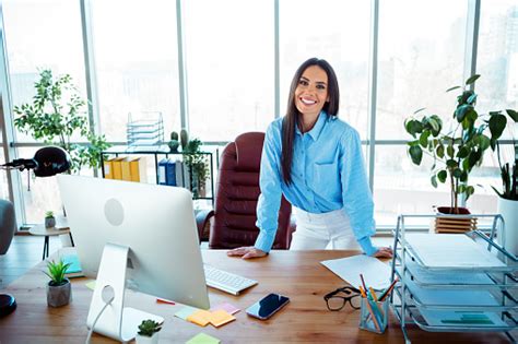 자신감 넘치는 젊은 전문직 여성이 밝은 곳에서 책상 옆에 서서 현대적인 사무실 환경에서 미소 짓고 있습니다 30 34세에 대한 스톡 사진 및 기타 이미지 Istock