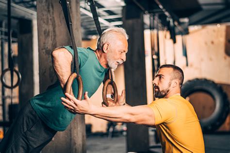 크로스핏 체육관 경기장에서 개인 피트니스 트레이너의 도움으로 체조 링에서 운동을하는 활동적인 노인 스포츠맨 2명에 대한 스톡 사진 및 기타 이미지 Istock