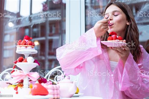 테이블에서 카페에서 야외에서 비옷에 앉아있는 행복한 예쁜 소녀는 달콤한 케이크와 음료를 제공하고 숟가락으로 식욕을 돋우는 베리 디저트로 먹는 즐거움을 선사합니다 귀여운 휴일