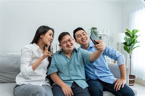 전화를 사용하는 자폐증을 가진 아시아 부모와 아들은 집에서 셀카를 찍습니다 행복한 가족 아름다운 사랑하는 어머니와 아버지는 젊은 남자와 함께 소파에 앉아 집에서 함께 스마트