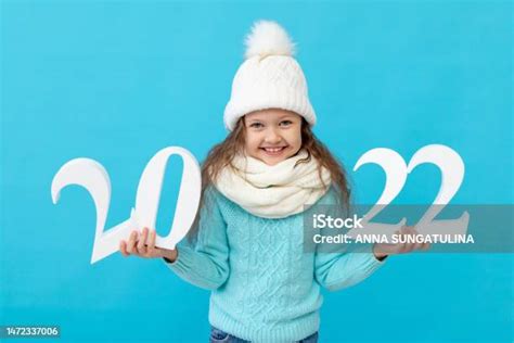 파란 고립 된 배경에 겨울 옷 모자와 스웨터에 미소 어린 소녀는 새해 2022의 숫자를 보유하고 미소 텍스트 장소 또는 공간을 보유하고 6 7 살에 대한 스톡 사진 및 기타