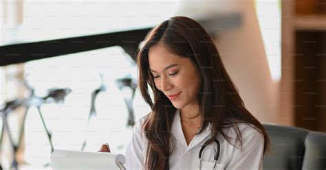 행복한 젊은 여성 의사는 증상 진단 서류를 보고 책상에서 의료 클립보드에 메모를 하고 있다 사진 Unsplash의 여성 의사 이미지