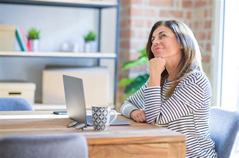 질문에 대해 생각 하는 컴퓨터 노트북 심각한 얼굴을 사용 하 여 집에서 테이블에 앉아 중년 노인 여자 매우 혼란 스러운 아이디어 갈색 머리에 대한 스톡 사진 및 기타 이미지