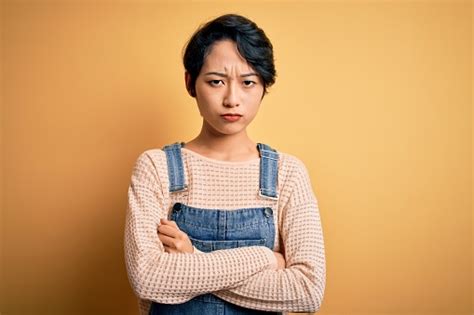 젊은 아름 다운 아시아 여자 캐주얼 데님 바지 위에 고립 된 노란색 배경 회의적이 고 긴장 교차 된 팔을 가진 얼굴에 표정을 거부 부정적인 사람 감정에 대한 스톡 사진 및