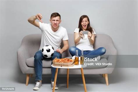 표현 커플 여자 남자 축구 팬은 회색 벽 배경에 고립 된 휴대 전화를 사용 하 여 엄지 손가락을 보여주는 지원 좋아하는 팀을 응원 사람들의 감정 스포츠 가족 레저 라이프