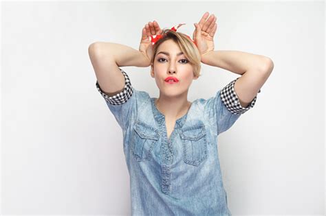 메이크업과 빨간 머리 띠와 함께 캐주얼 블루 데님 셔츠에 재미 있는 아름 다운 젊은 여자의 초상화 서와 토끼 귀 제스처 손 카메라를 보고 교습에 대한 스톡 사진 및 기타