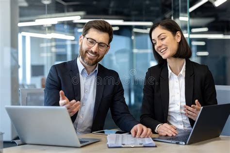 Business Colleagues Discussing Work Ideas Using Laptops In Modern Office Environment With