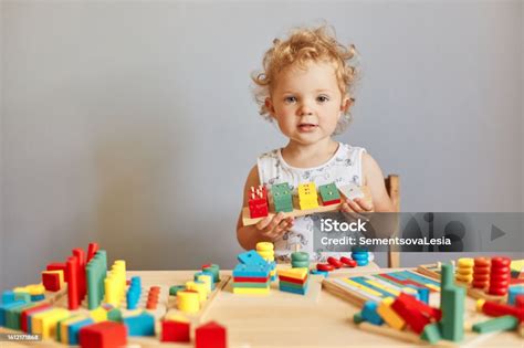 유아의 즐거운 학습 경험 유아의 호기심 많은 탐험 아이의 상상력이 풍부한 놀이 시간 회색 배경 위에 고립된 나무 교육 장난감을 가지고 노는 재미있는 물결 모양의 금발 유아