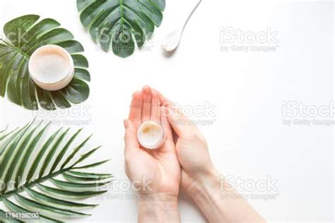 플랫레이 미용 크림 잎 야자수 가지의 항아리 중 흰색 배경에 그녀의 손에 영양 크림을 넣어 여자 매니큐어의 마지막 단계 여성은 피부에 보습제를 사용합니다 공간을 복사합니다