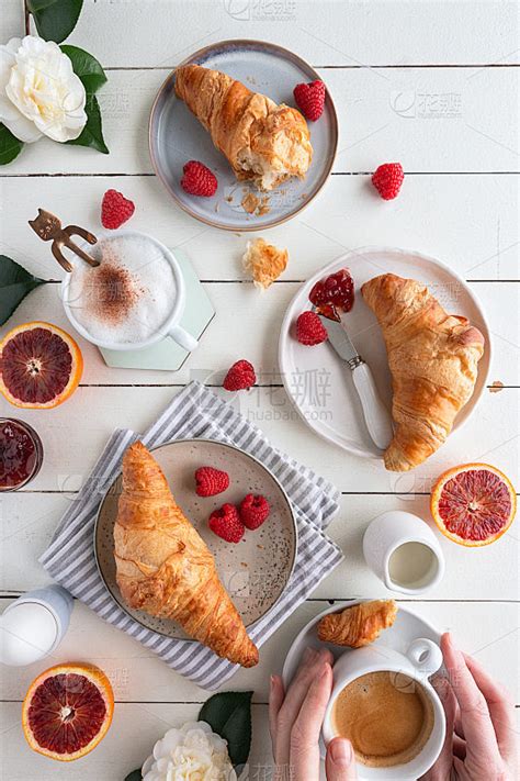 白色木桌上平铺着一张早餐桌，上面竖直摆放着羊角面包、咖啡、水果和鲜花