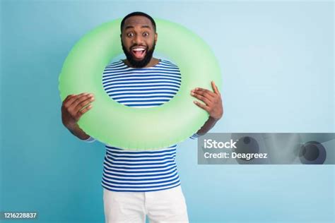 명랑한 어두운 피부 남자 보유 녹색 생활 부표 목 준비 수영 바다 여행자 좋은 분위기 화창한 날 착용 스트라이프 선원 셔츠 고립 된 블루 컬러 배경 갈색 머리에 대한 스톡